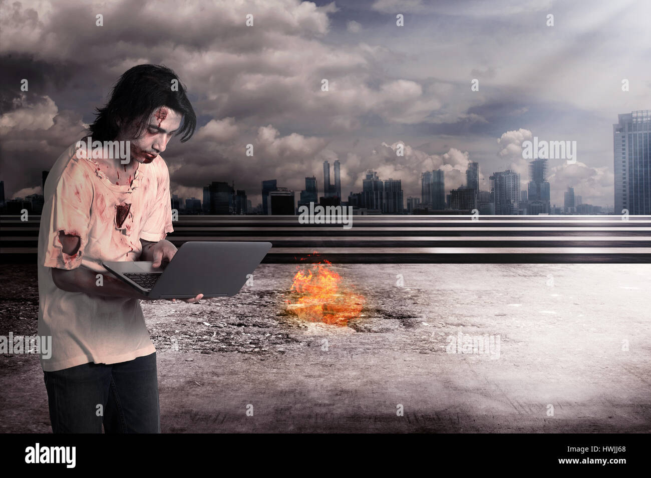 Creepy male zombie typing with laptop with city on fire background ...