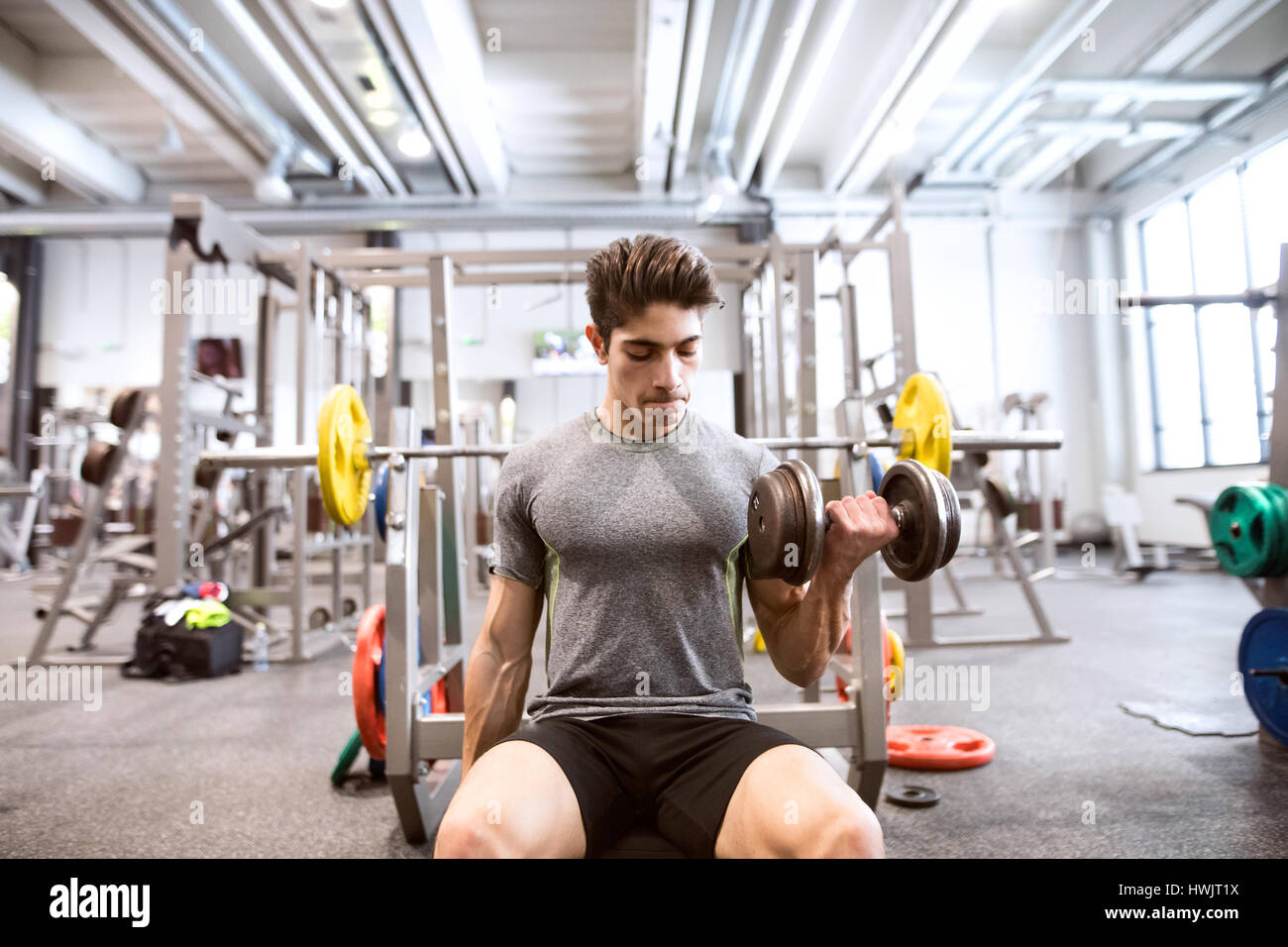 Young hispanic fitness man in gym sitting on bench, working out with ...