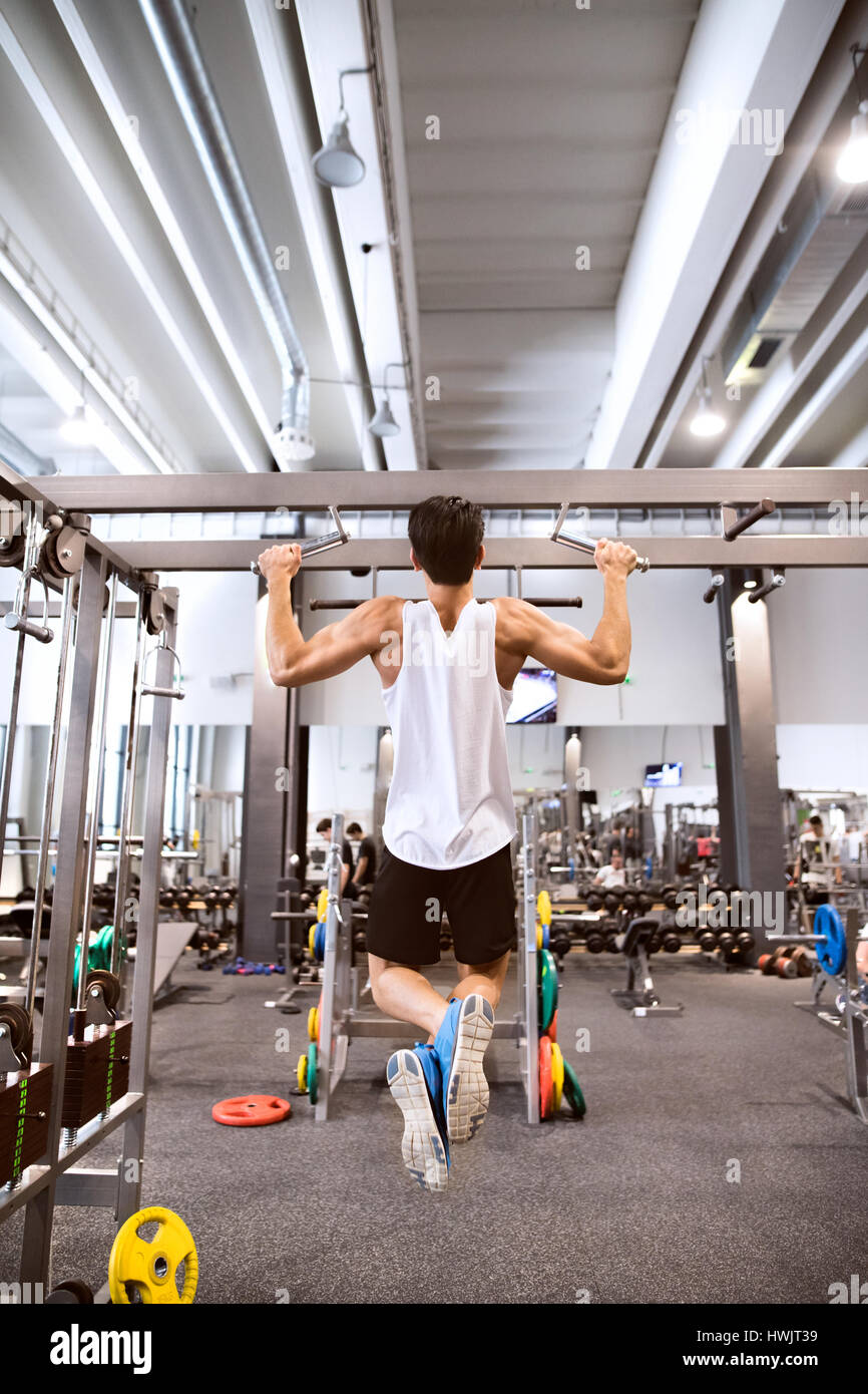 Young hispanic fitness man in gym working out, doing pull-ups on ...