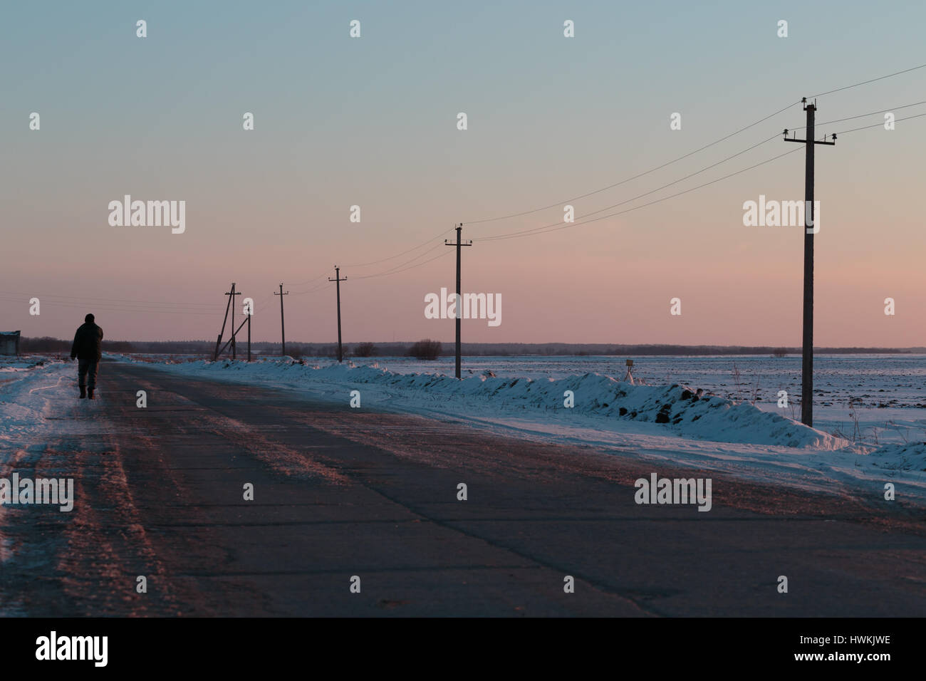lonely man walks along a deserted winter road at sunset.Russian road in ...