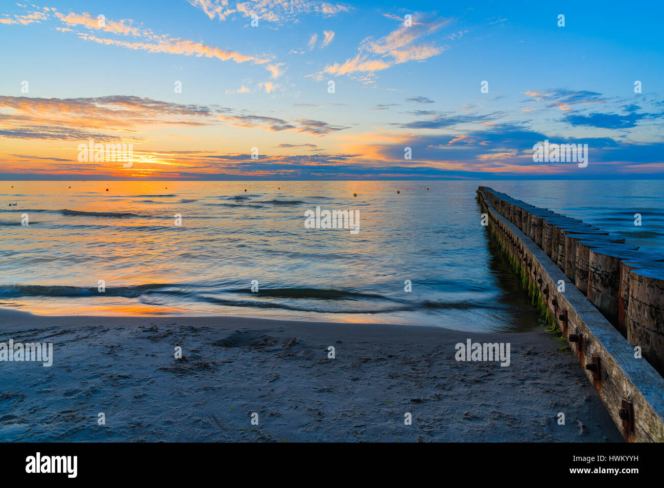 Sunset over sea with wooden breakwaters in foreground on Leba beach ...