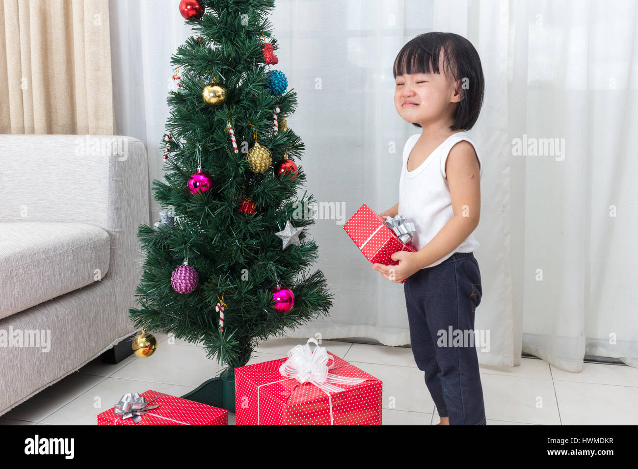 Asian Chinese little girl holding gift box crying beside Christmas tree ...