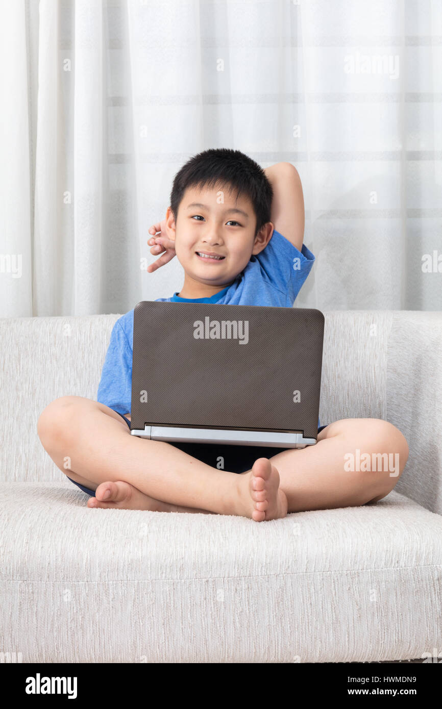 Happy Asian Chinese little boy using laptop on the sofa in the living ...