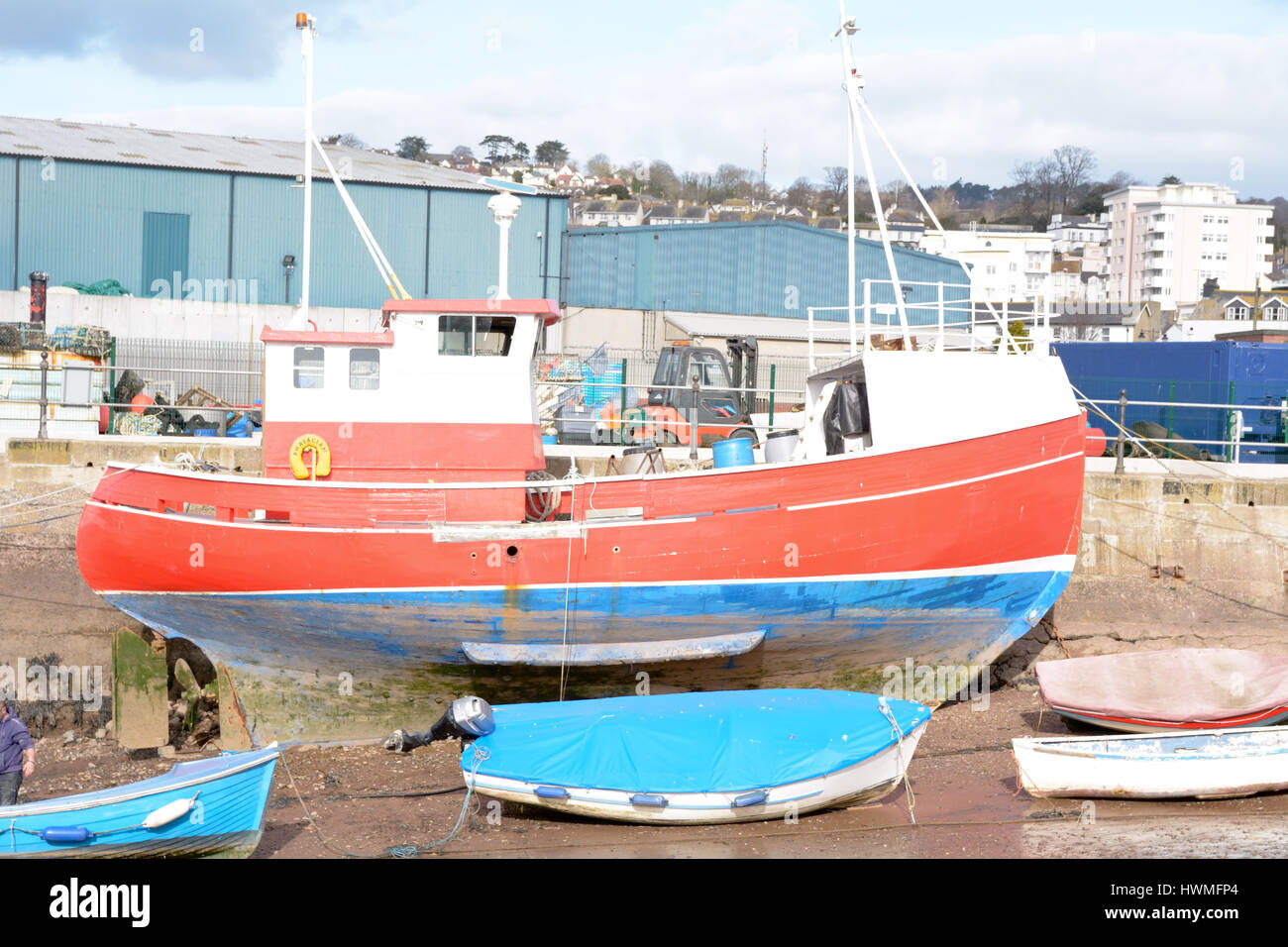 Small trawler boat painted red white and blue moored to sea wall at low ...