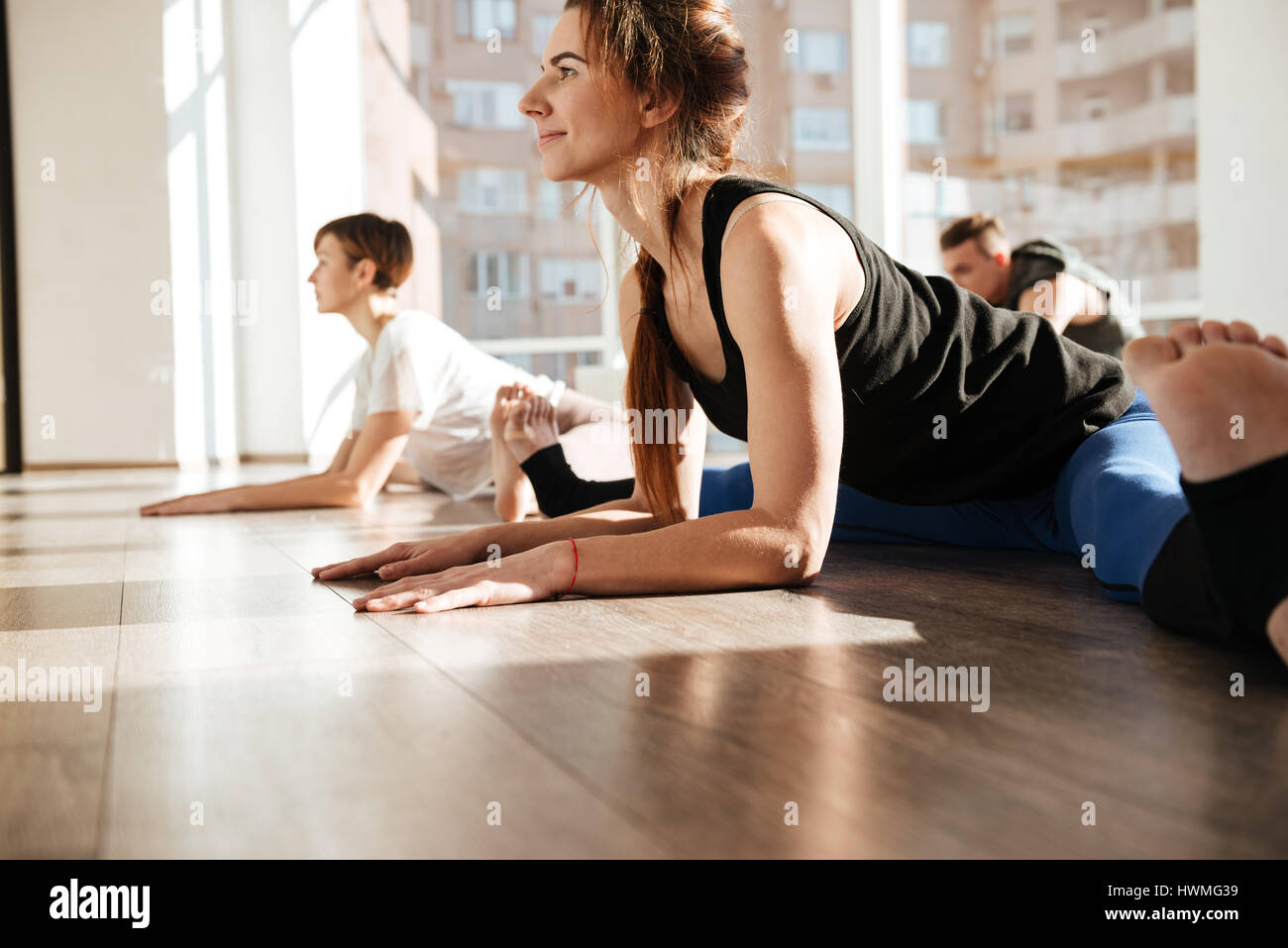 Happy young woman doing twine and stretching in group in yoga studio ...