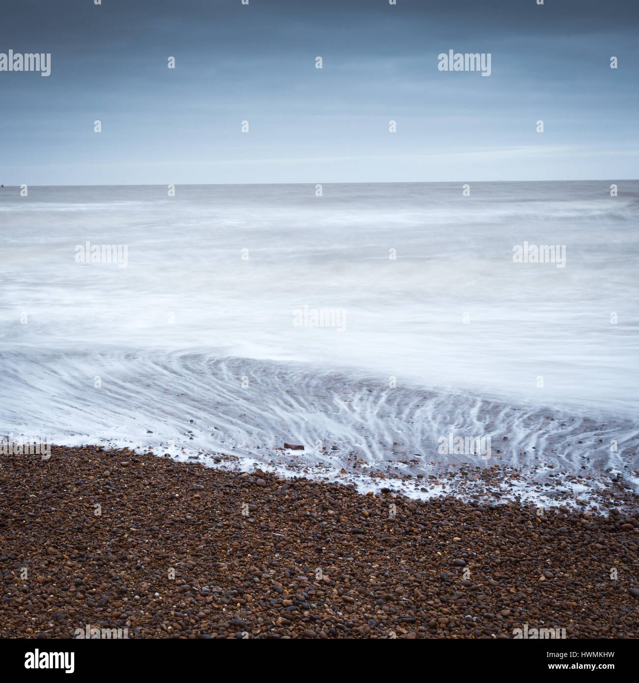 Minimalist morning sunrise seascape with shingle beach and blue sky at ...