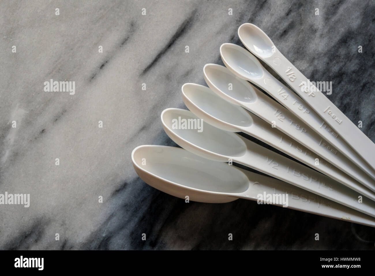 Set of white plastic measuring spoons in a fan shape showig imperial ...