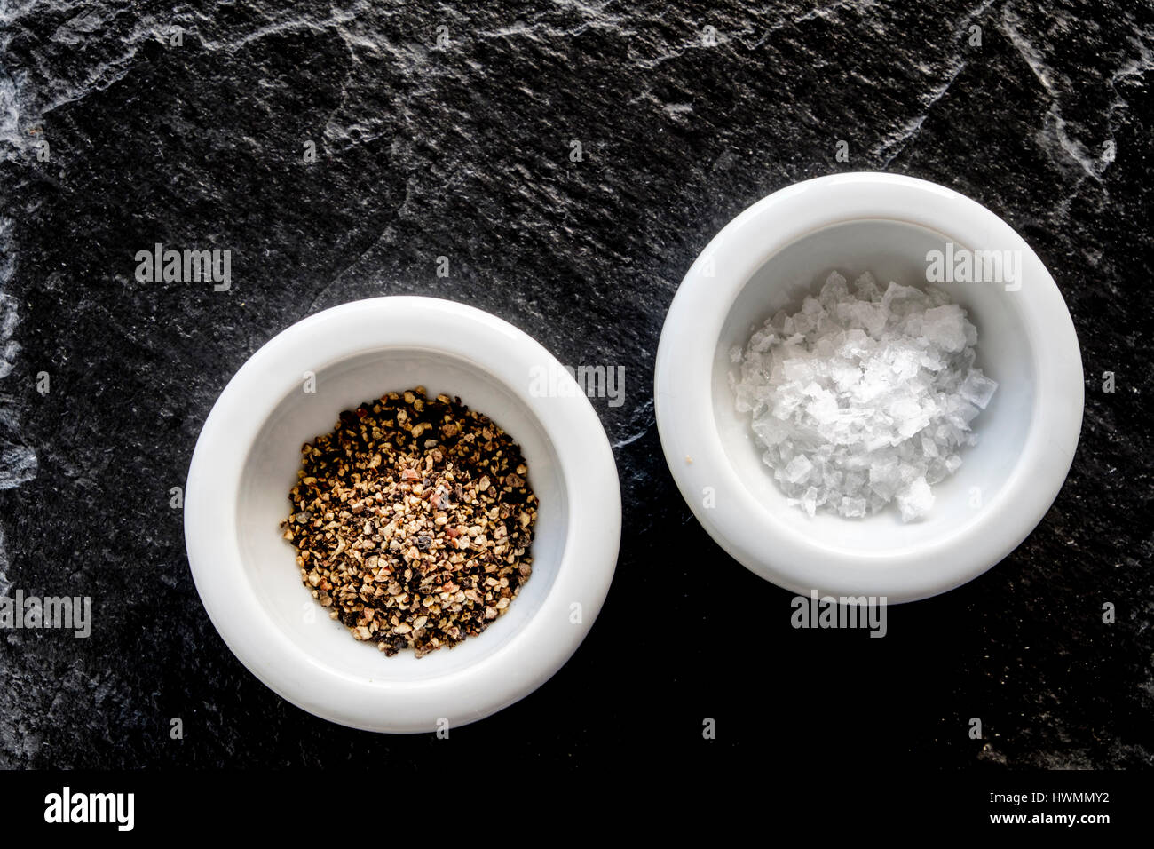 Two small white dishes of sea salt flakes and freshly ground black ...
