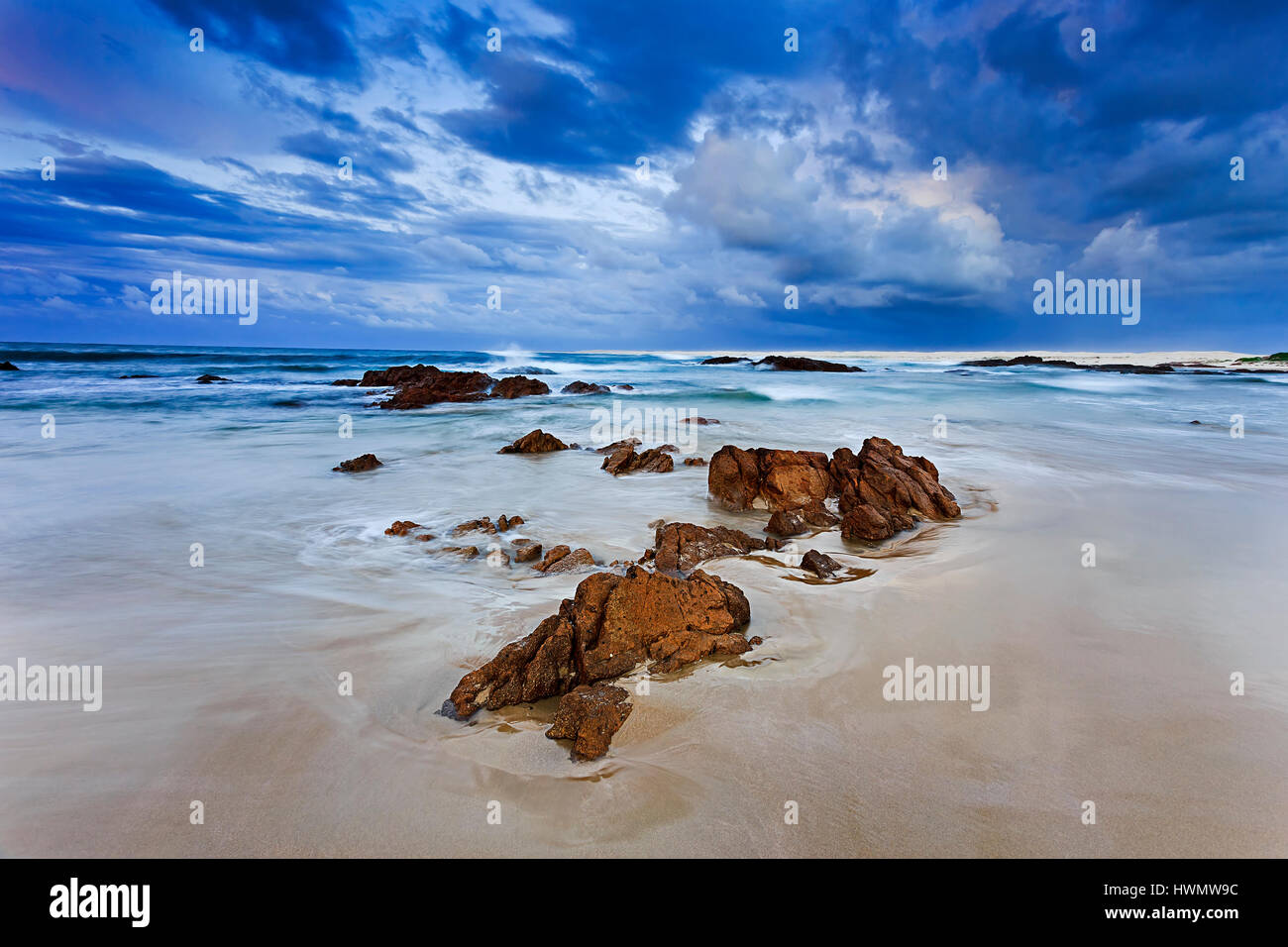 Calm blue sunrise at white sand beach with small sandstone rocks at low ...