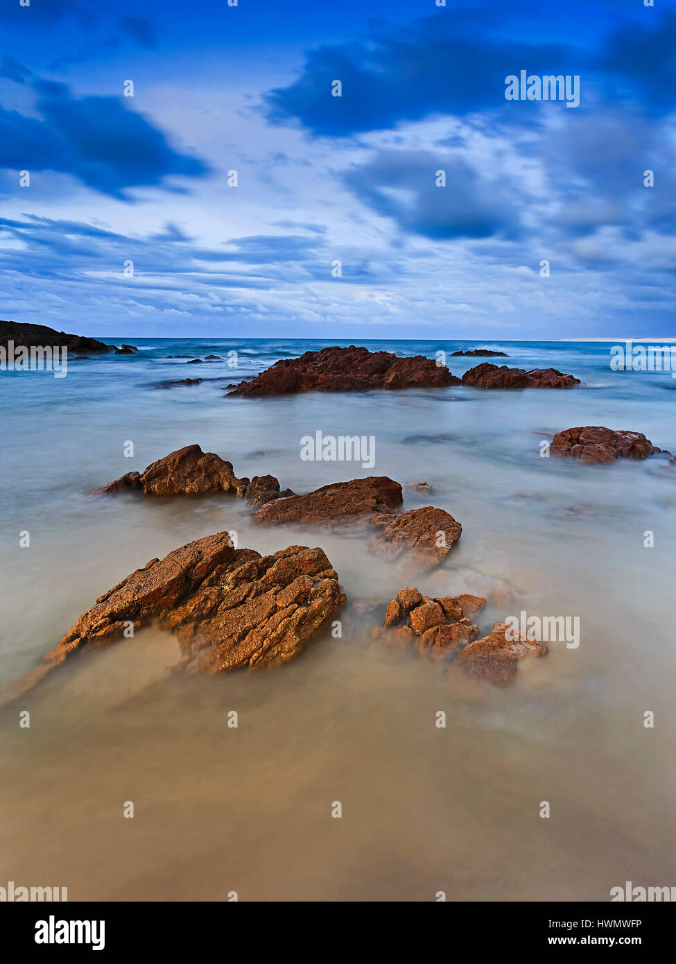 Small sandstone rocks standing out from tiding surfing waves blurred at ...