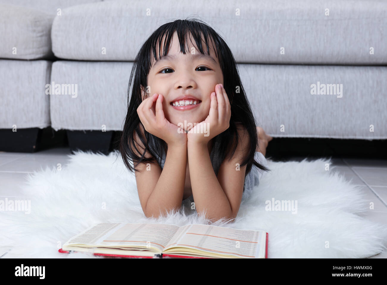 Happy Asian Chinese little girl reading book on the floor in the living ...