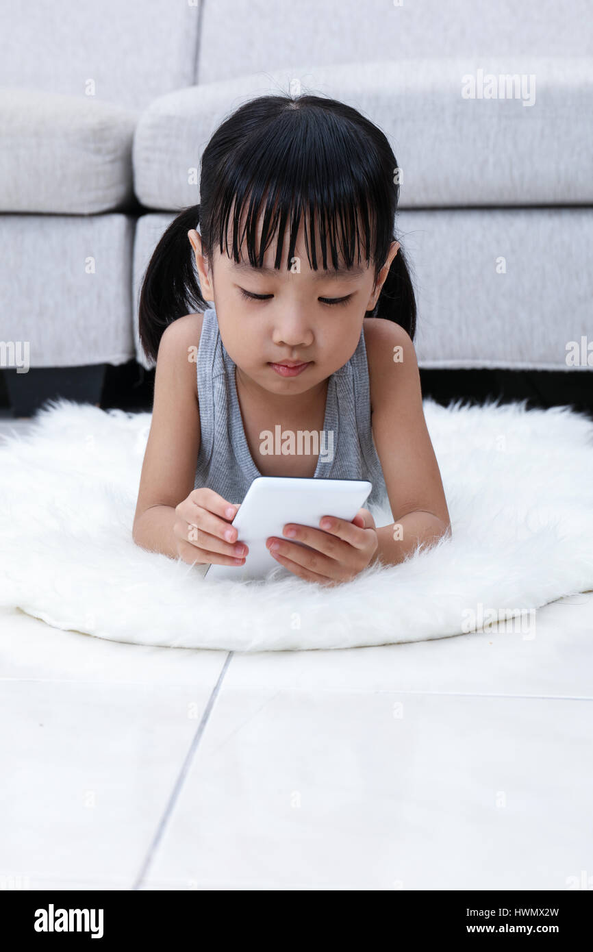 Asian Chinese little girl playing phone on the floor in the living room ...