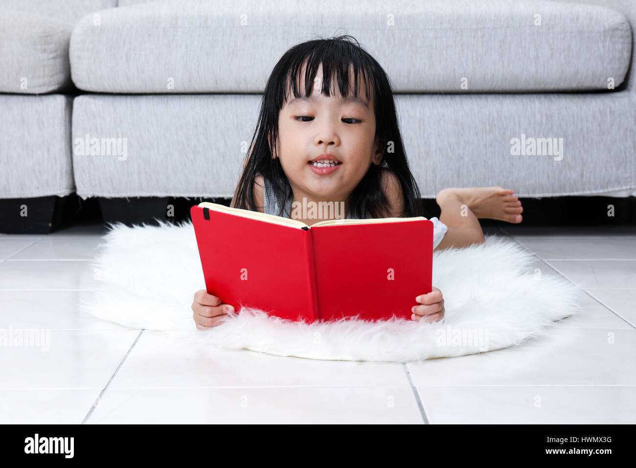Asian Chinese little girl reading book on the floor in the living room ...