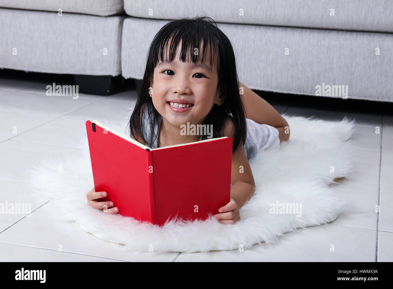 Happy Asian Chinese little girl reading book on the floor in the living ...
