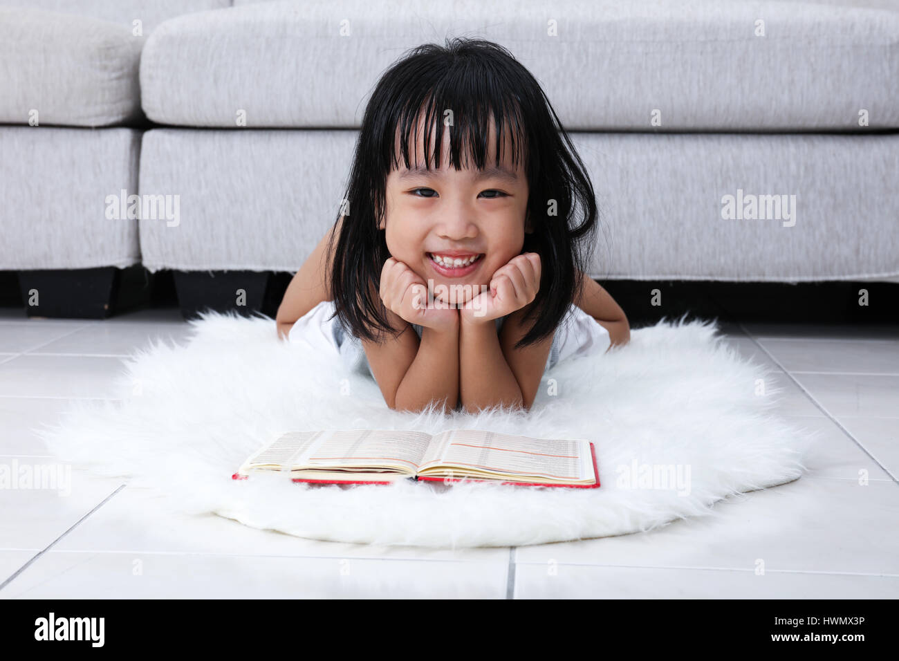 Happy Asian Chinese little girl reading book on the floor in the living ...