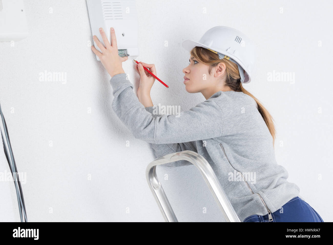 Woman marking position for alarm on wall Stock Photo - Alamy