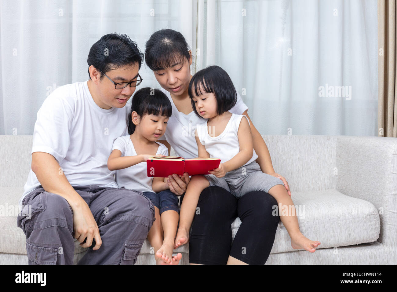 Asian Chinese parents and daughters reading book on the sofa in the ...