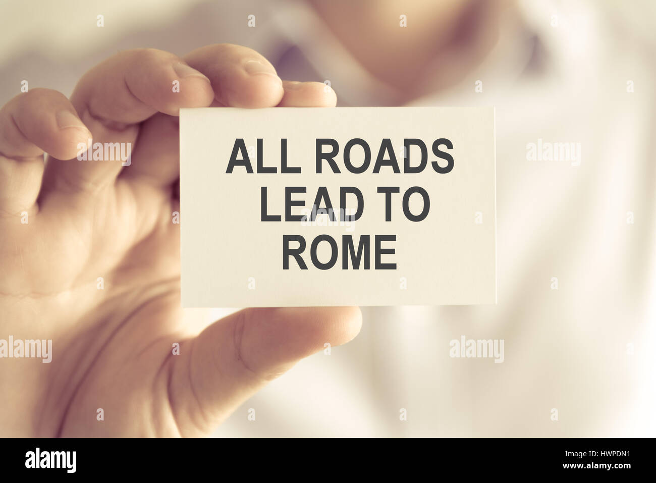 Closeup on businessman holding a card with text ALL ROADS LEAD TO ROME ...