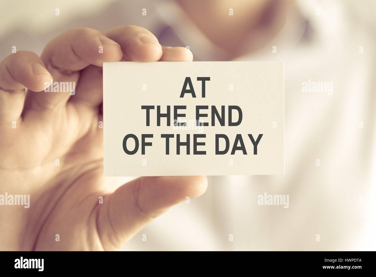 Closeup on businessman holding a card with text AT THE END OF THE DAY ...