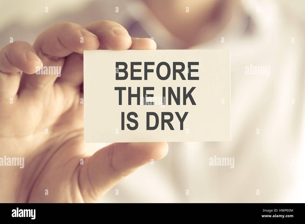Closeup on businessman holding a card with text BEFORE THE INK IS DRY ...