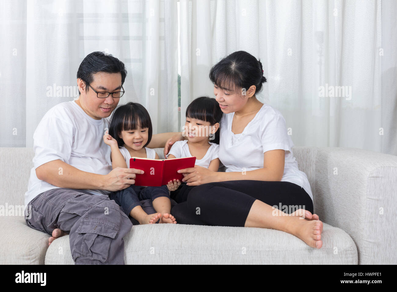Happy Asian Chinese family reading book on the couch in the living room ...