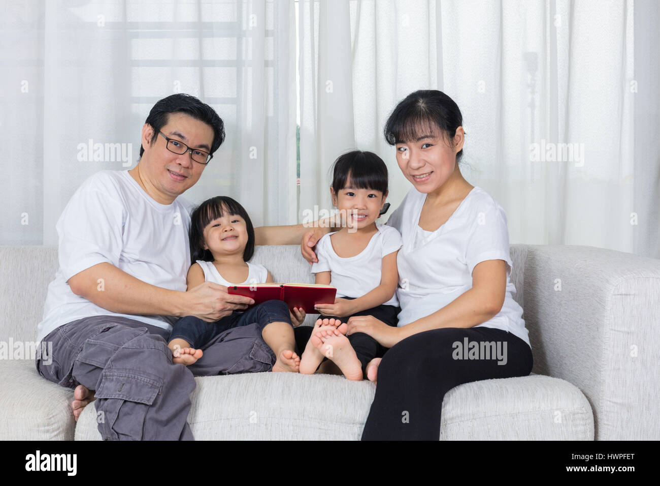 Happy Asian Chinese family reading book on the couch in the living room ...