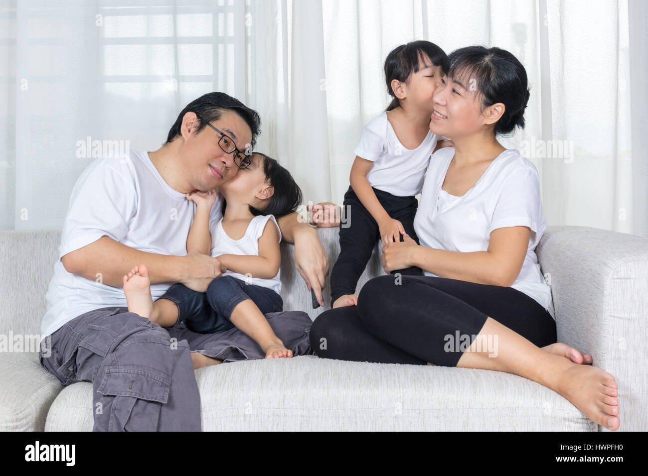 Happy Asian Chinese family kissing on the couch in the living room at ...