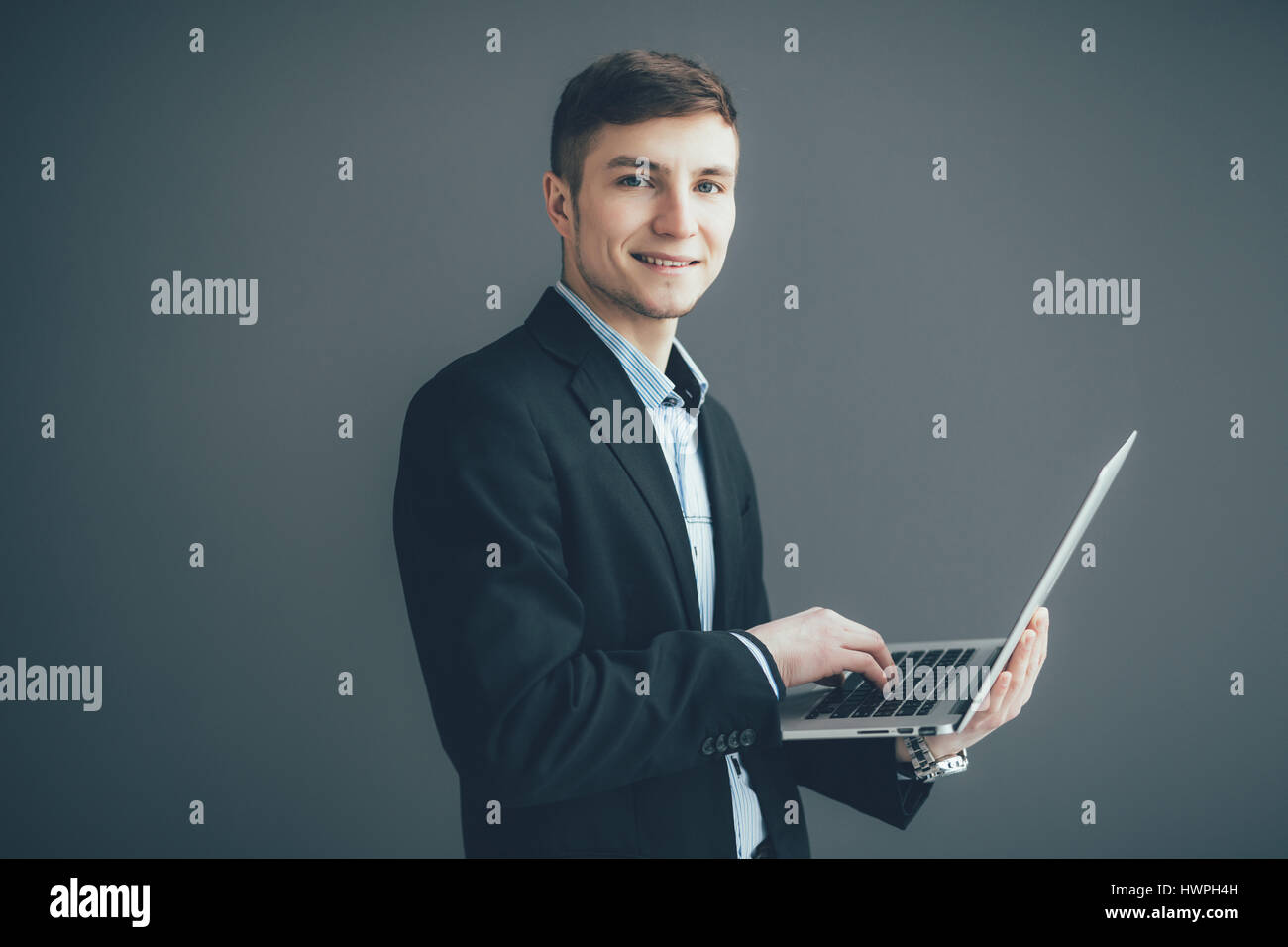 Handsome young businessman is using a laptop, looking at camera and ...