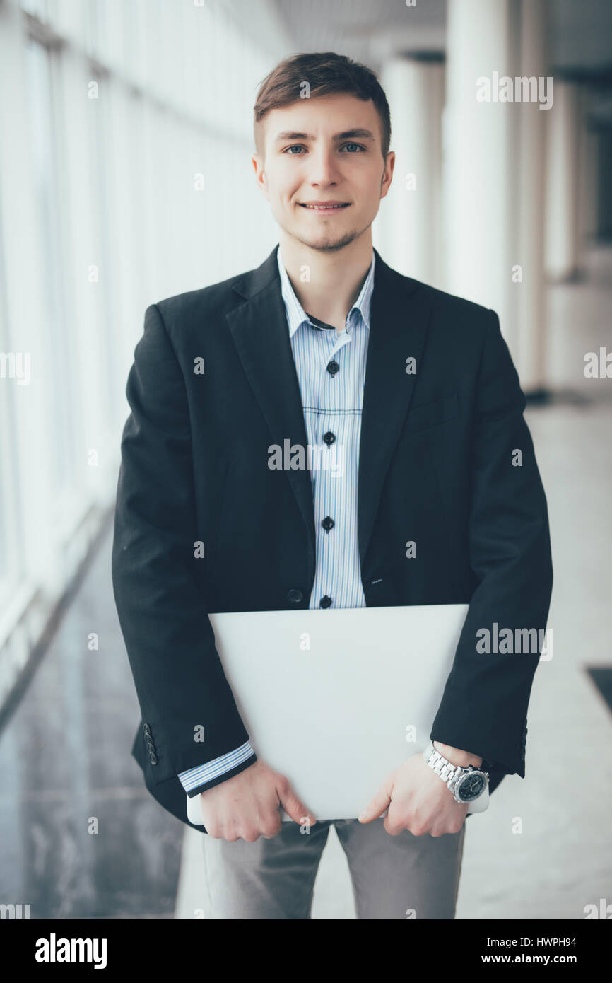 Serious businessman walking with laptop in hands in office Stock Photo ...