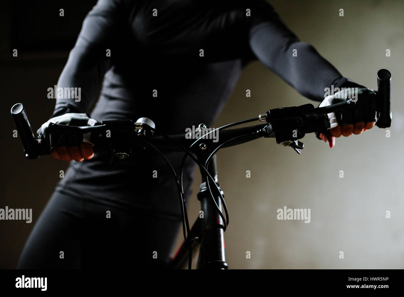 cycle man with bike indoors. Man in black cycling Apparel on gray wall ...