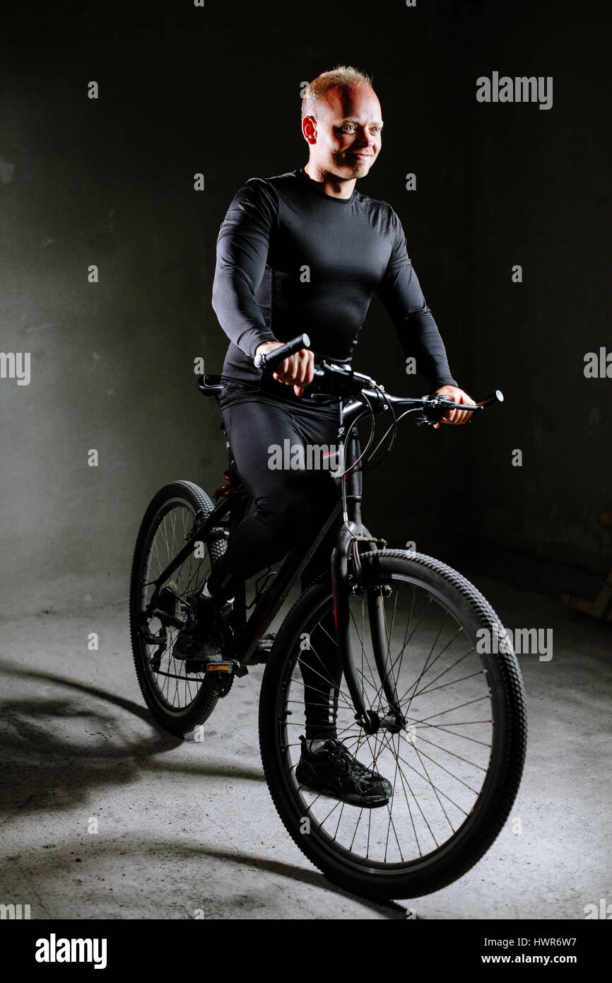cycle man with bike indoors. Man in black cycling Apparel on gray wall ...