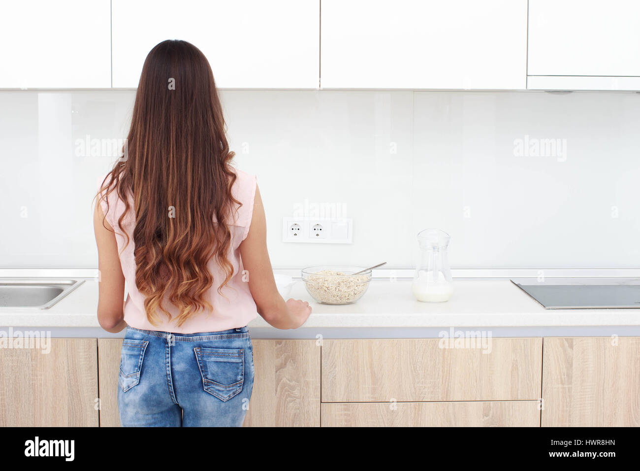 Back view of little girl with long curly hair standing at a kitchen ...