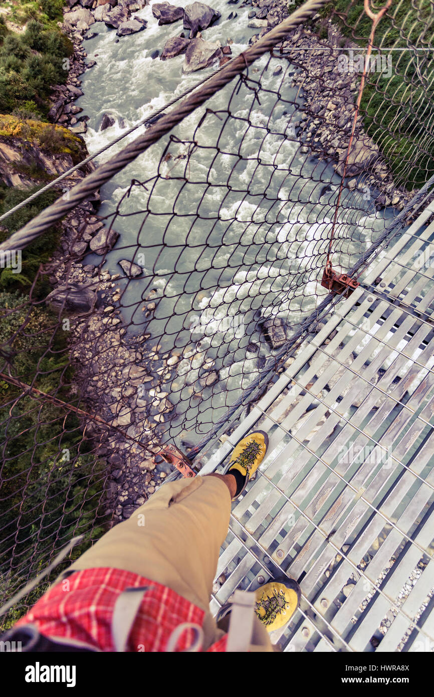 Backpacker crossing suspension bridge and looking down at the river in ...