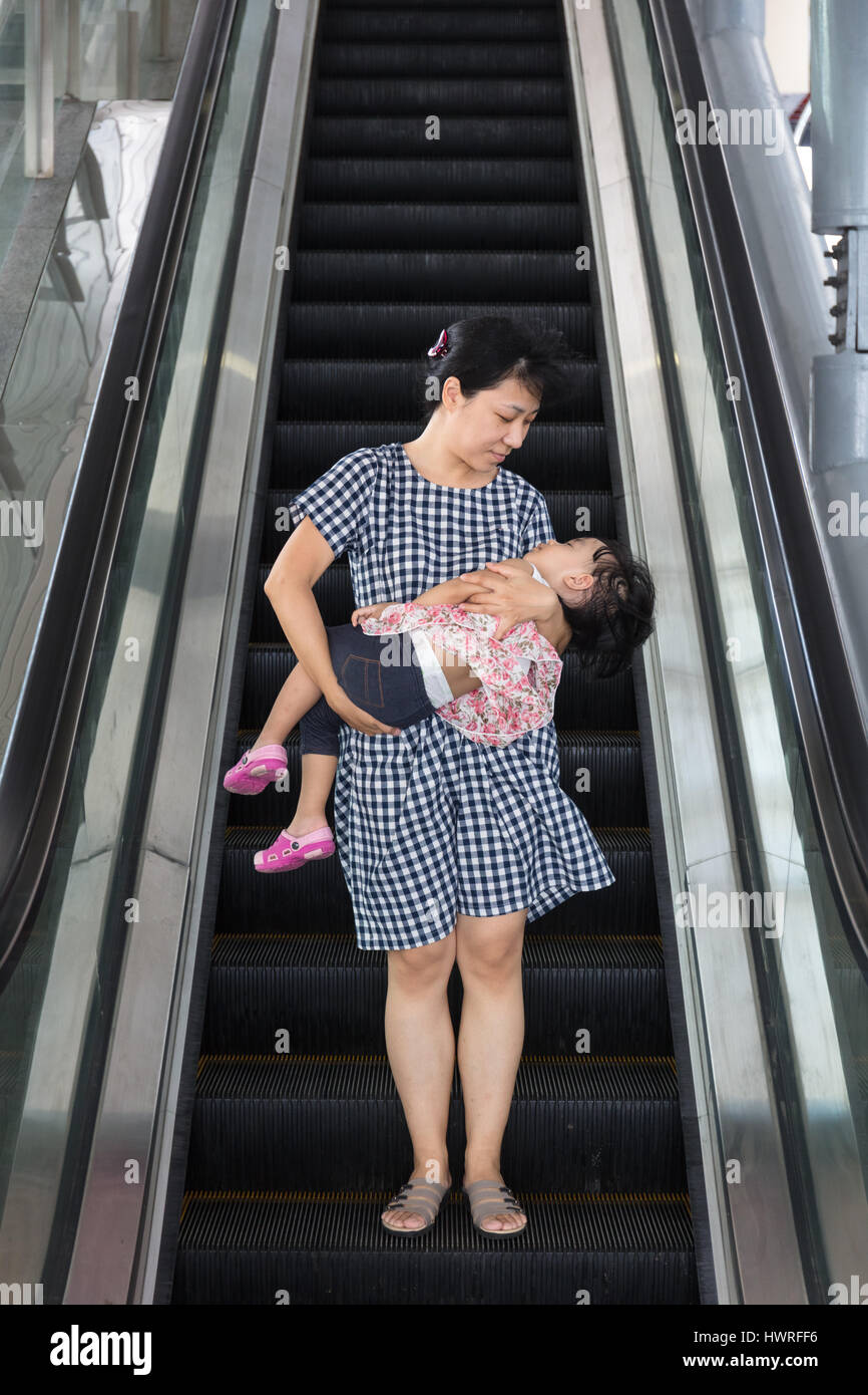 Asian Chinese mother carrying sleeping daughter taking escalator at MRT ...