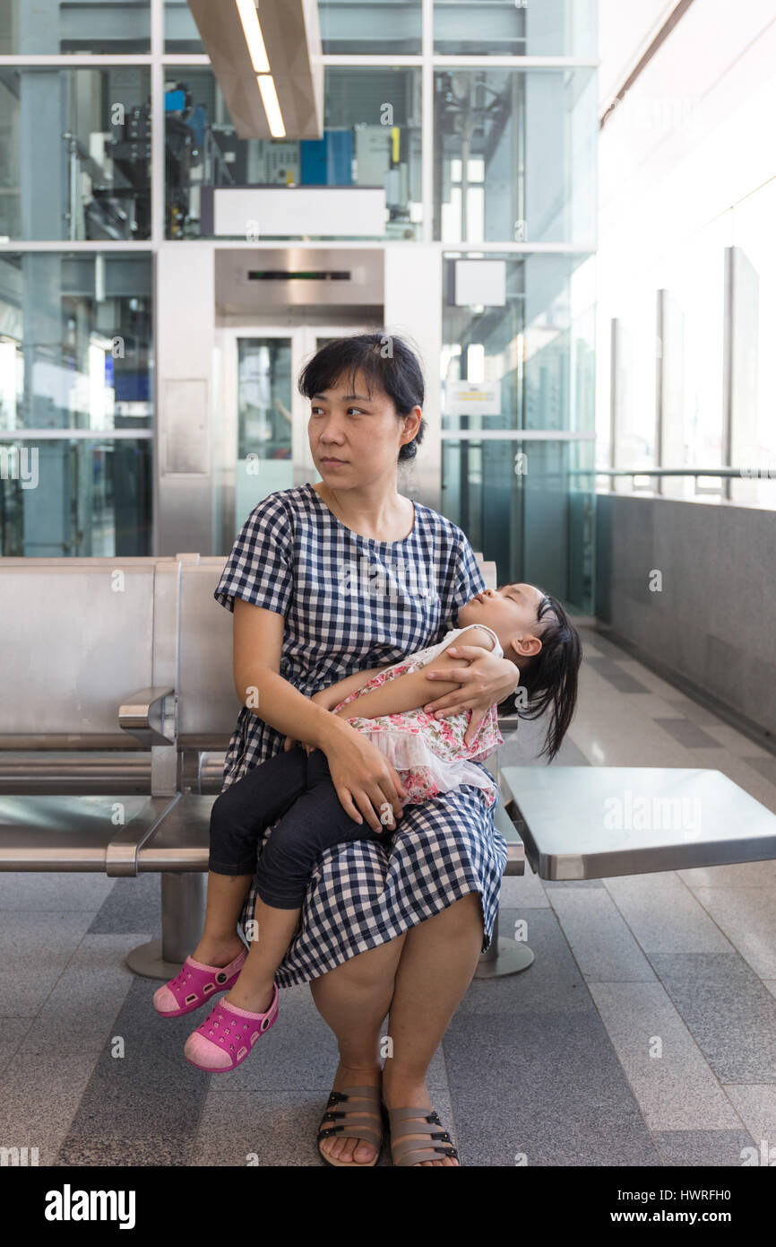 Asian Chinese mother carrying sleeping daughter inside a MRT station in ...