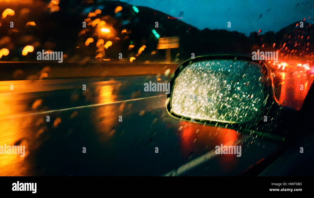 Side-view mirror seen through car window during rainy season at night ...