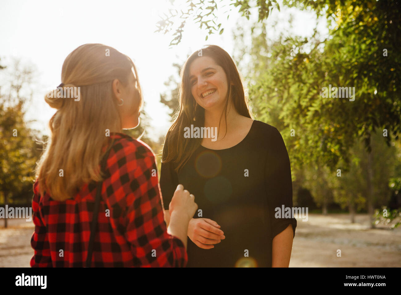 Female friends talking while standing at park Stock Photo - Alamy