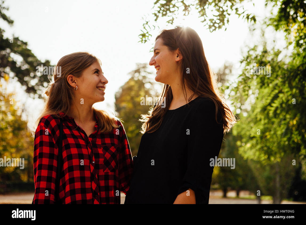 Smiling friends talking while standing at park Stock Photo - Alamy