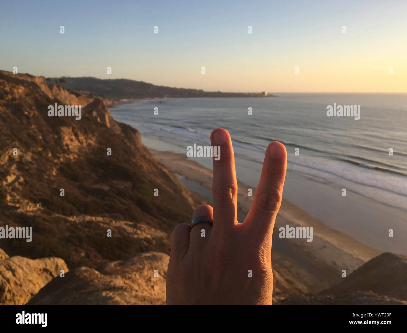 Cropped hand of man showing peace sign at beach against clear sky ...