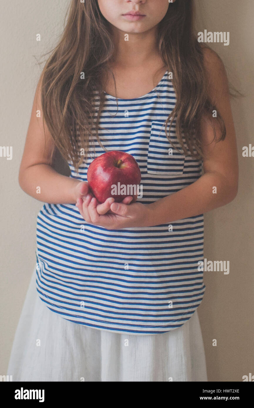 Midsection of girl holding apple while standing against wall at home ...