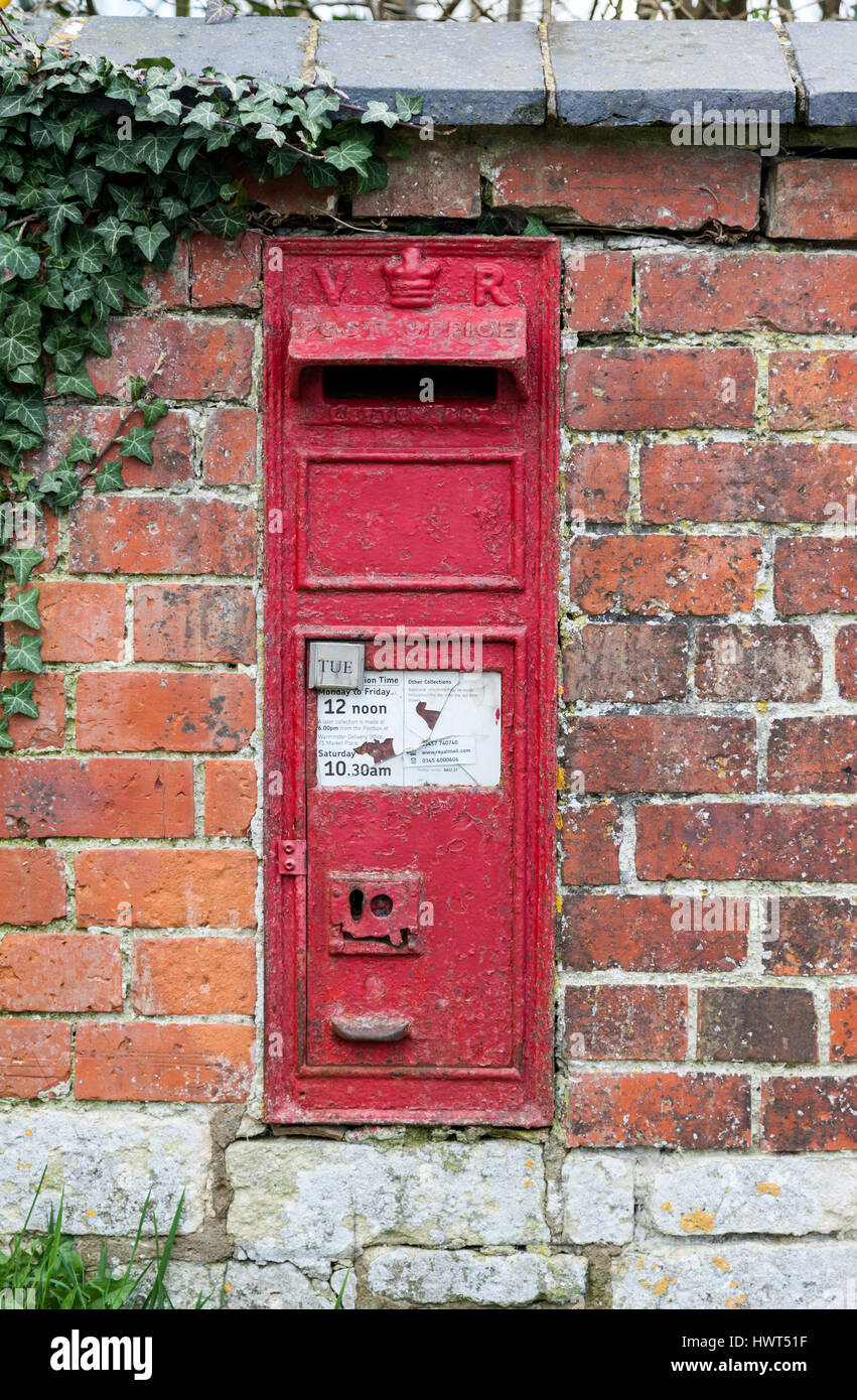 Traditional old red postbox situated in a red brick wall in the village ...