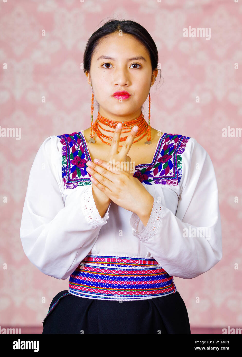 Young woman wearing traditional andean dress, facing camera doing sign ...