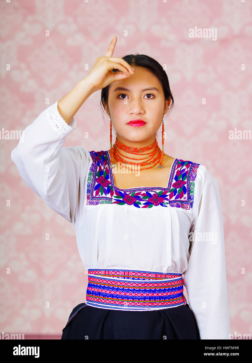 Young Woman Wearing Traditional Andean Dress Facing Camera Doing Sign 