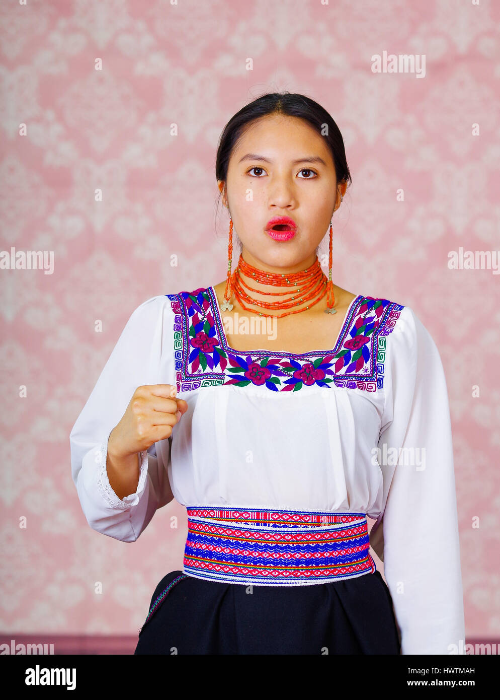 Young woman wearing traditional andean dress, facing camera doing sign ...