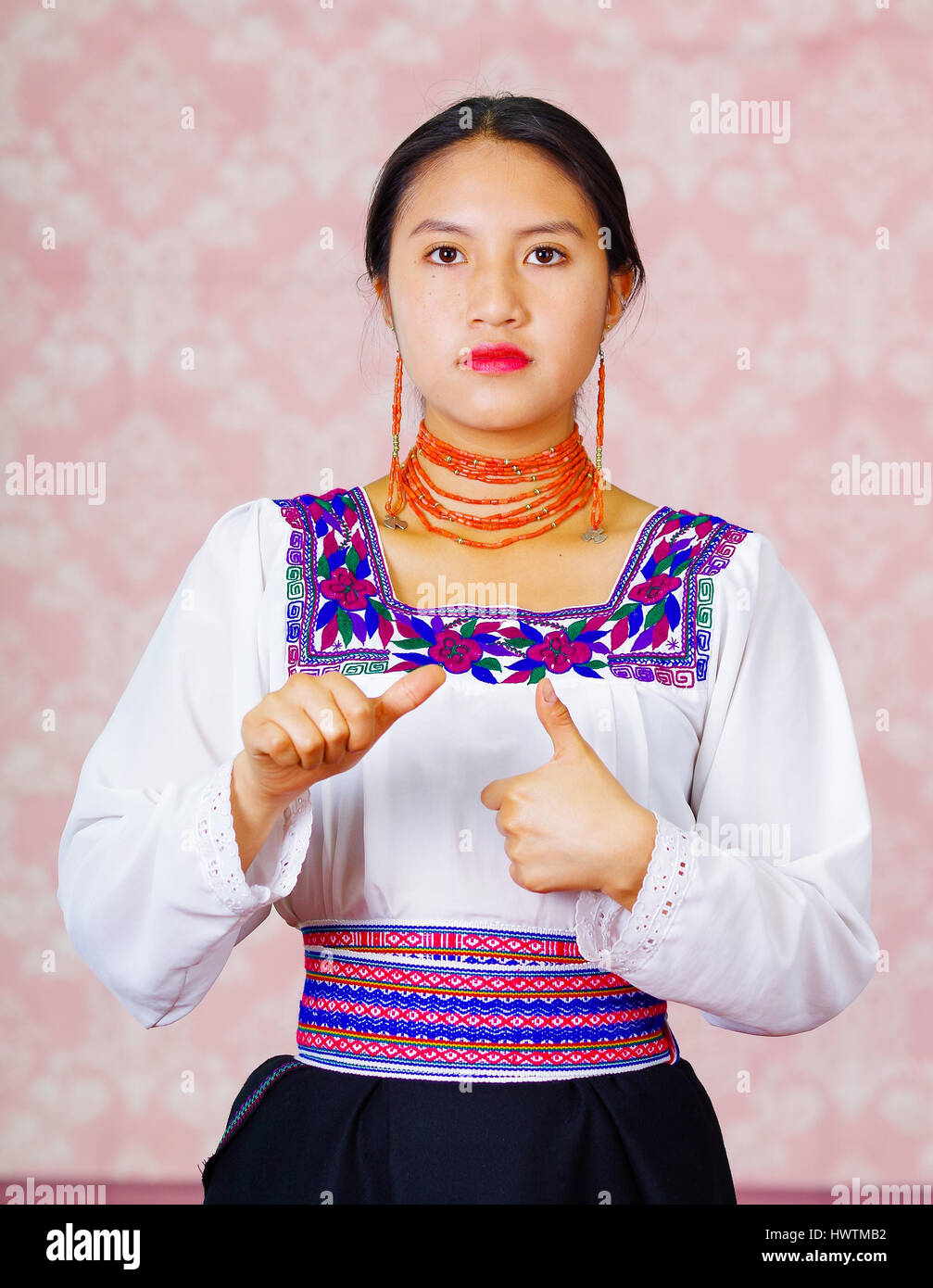 Young woman wearing traditional andean dress, facing camera doing sign ...