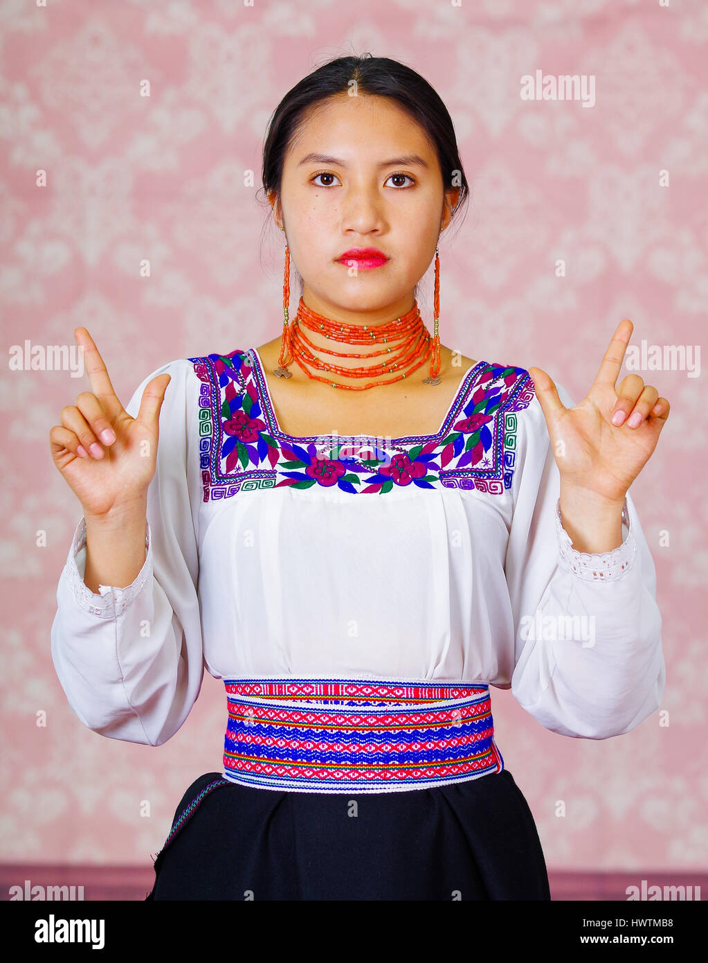 Young woman wearing traditional andean dress, facing camera doing sign ...