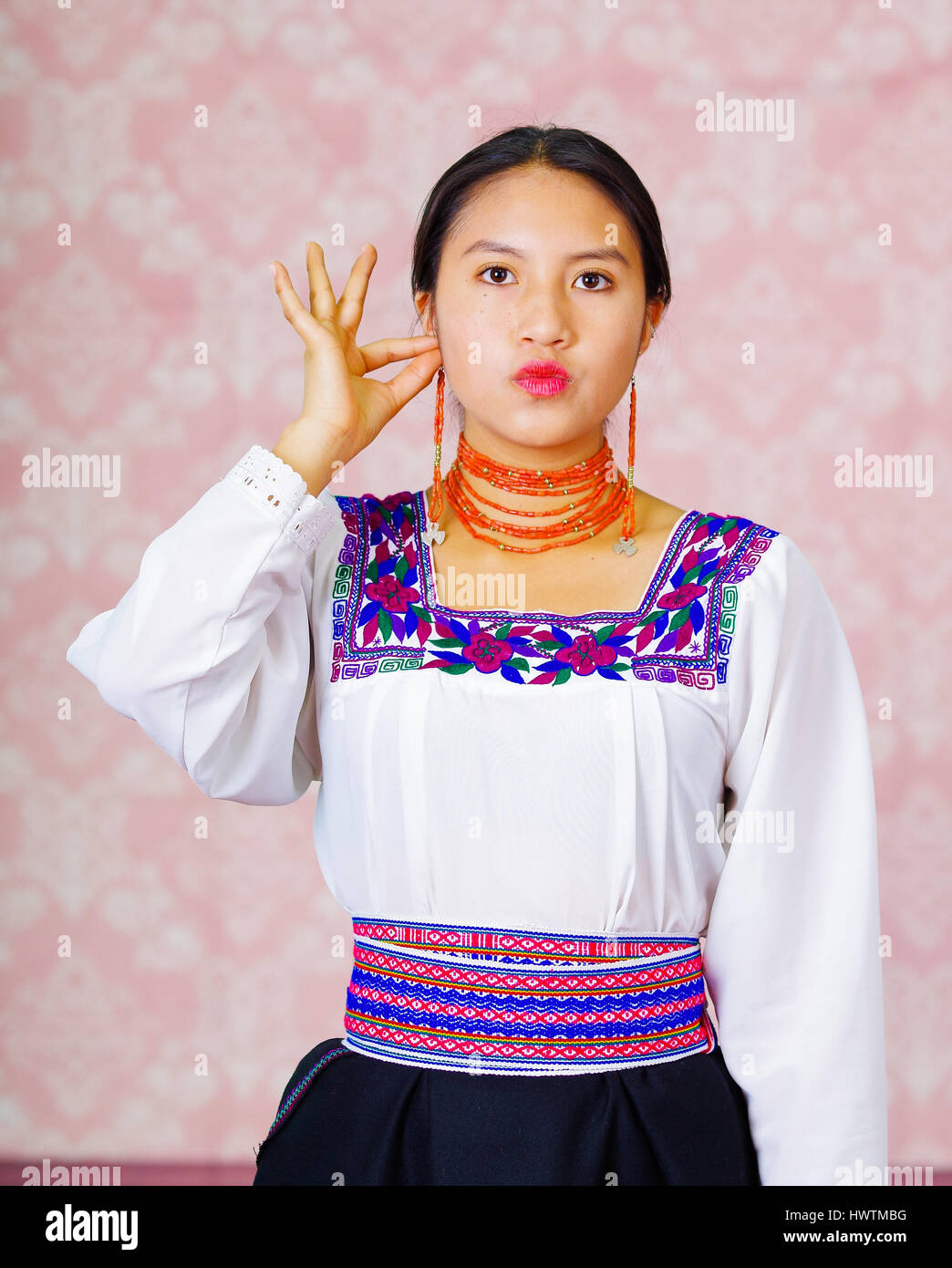 Young woman wearing traditional andean dress, facing camera doing sign ...