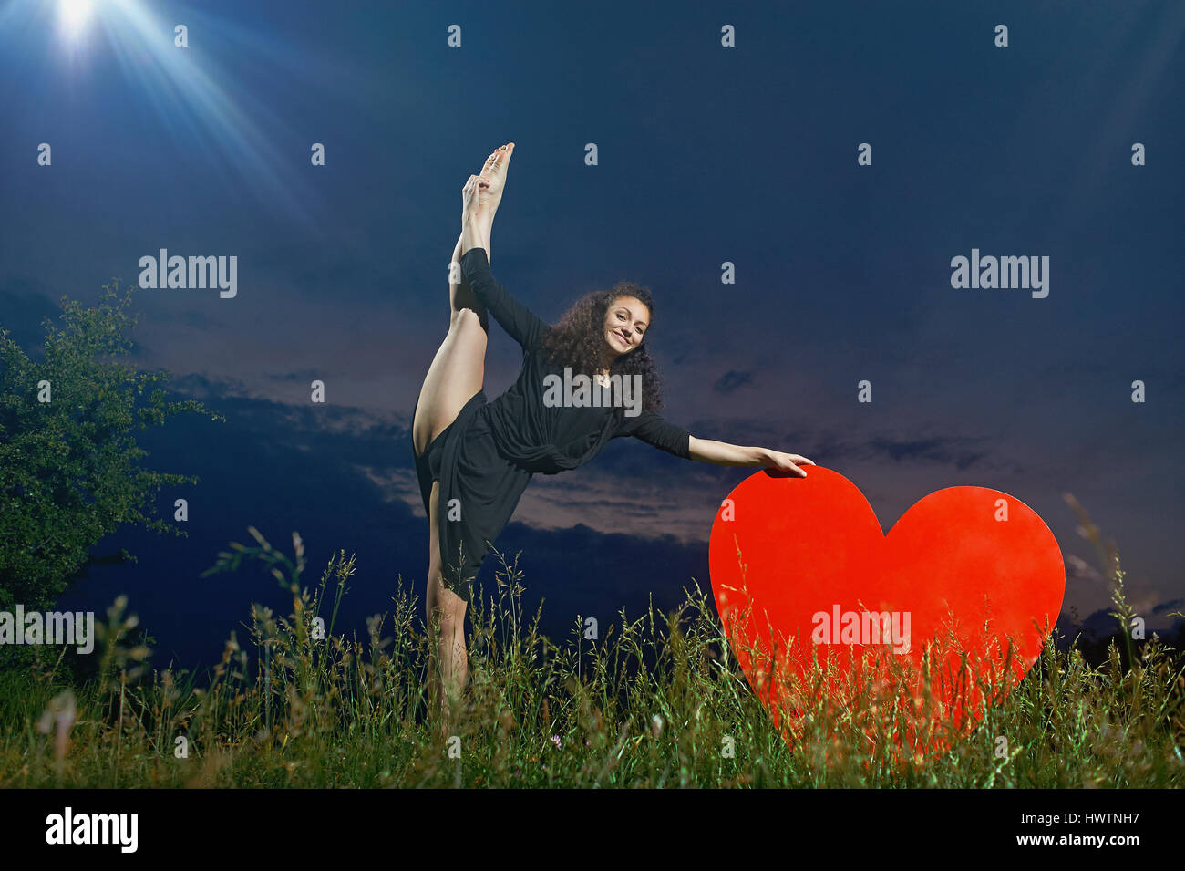 smiling, curly dancer performs vertical side splits in grassy field ...
