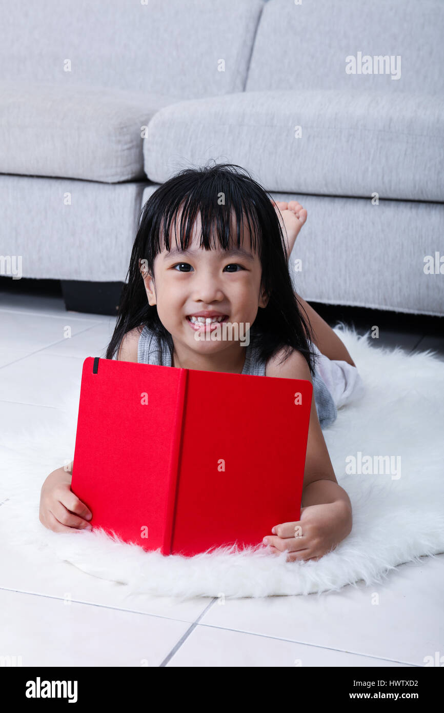 Happy Asian Chinese little girl reading book on the floor in the living ...