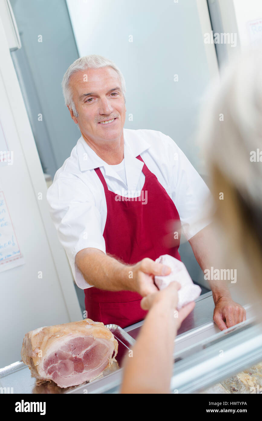 Butcher passing produce to customer Stock Photo - Alamy